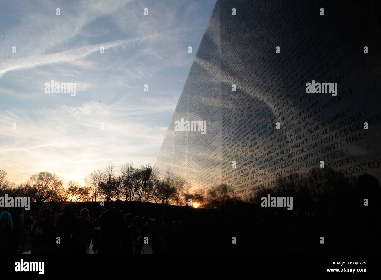 Tourists at the Vietnam War memorial at sunset. names on the wall ...