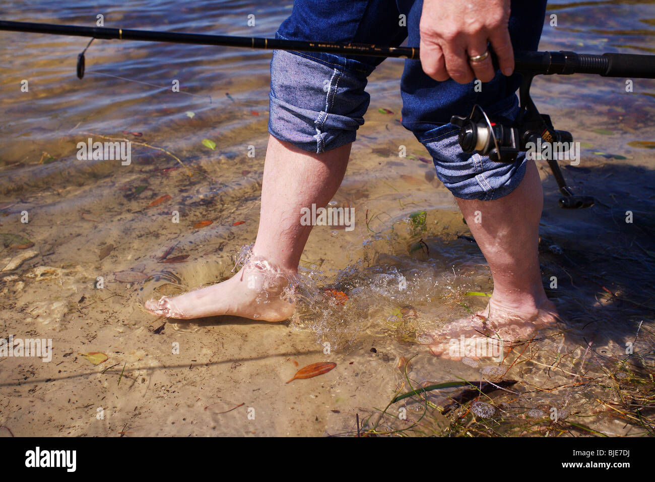 FISHERMAN STANDING IN SHALLOW WATER HOLDING FISHING ROD AND REEL BLUE ...