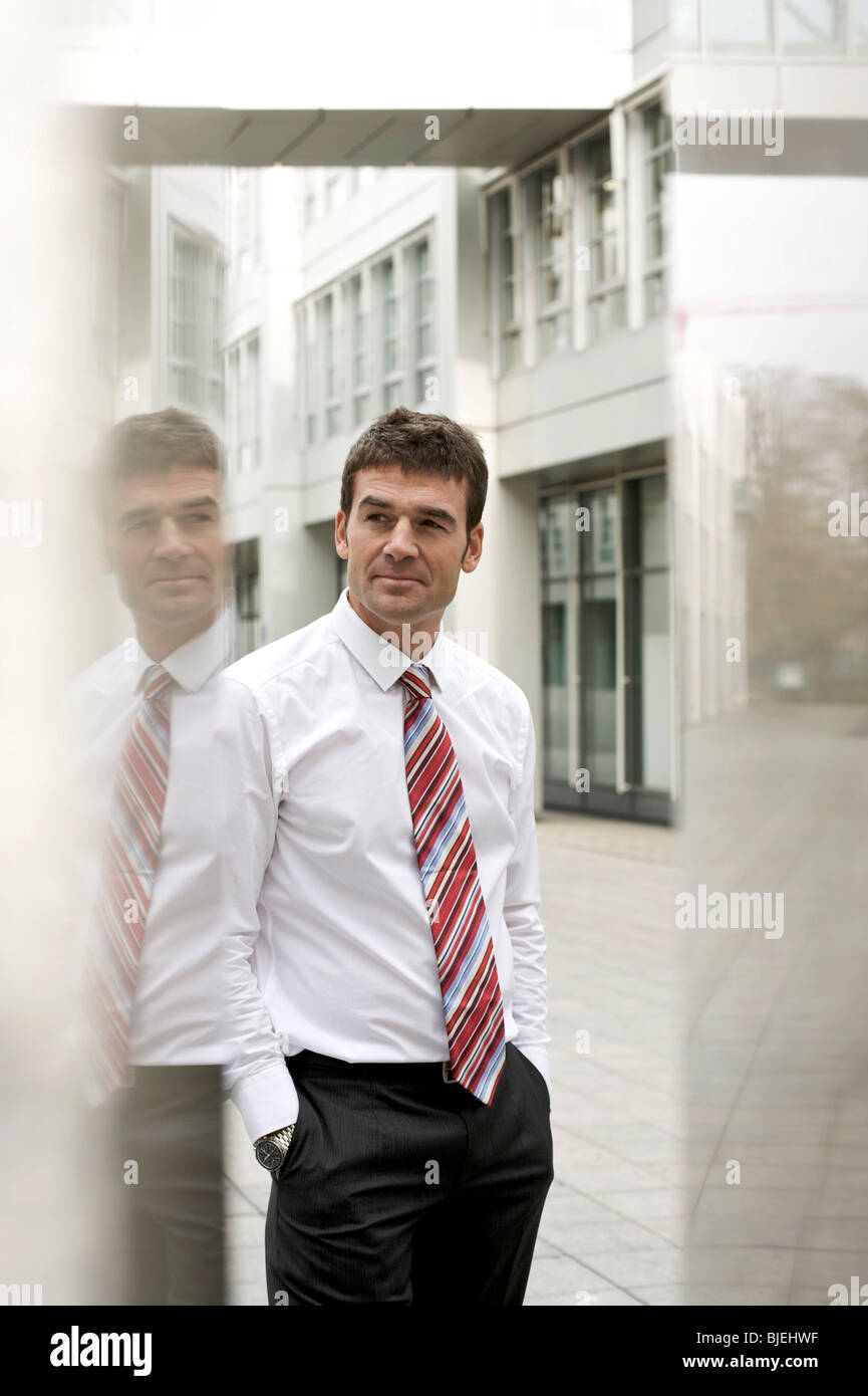 Businessman standing between reflective columns, three quarter length ...