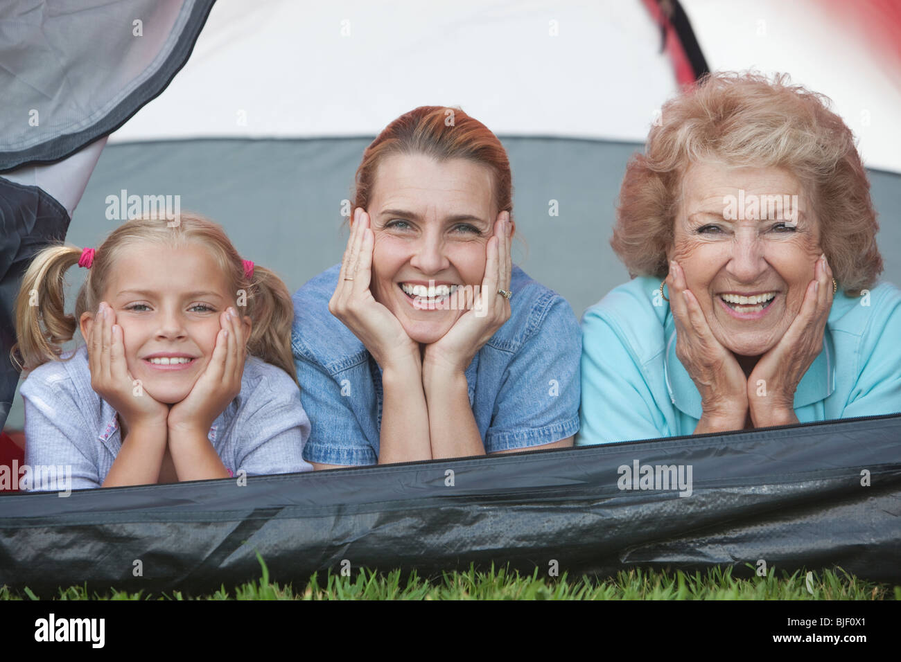 Mother, daughter and grand-daughter lean on elbows, smiling from tent ...