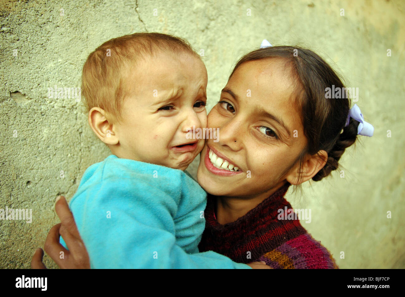 Baby brother crying elder sister laughing Stock Photo - Alamy