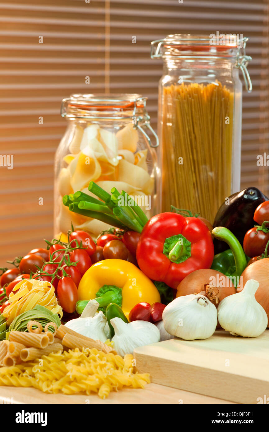 A selection of dried pasta loose and in jars and fresh vegetables ...
