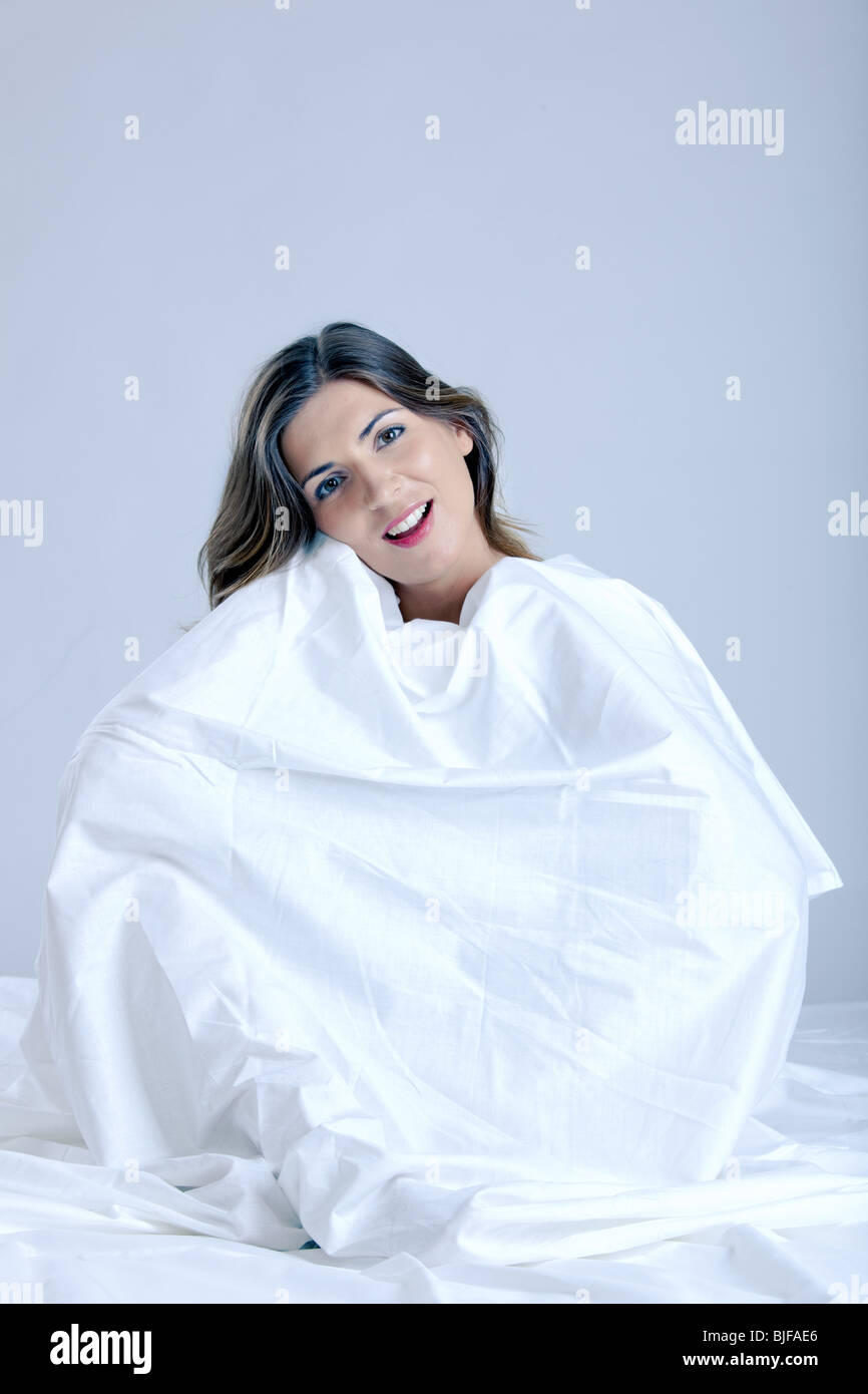 Beautiful young woman covered with white sheets on bed Stock Photo - Alamy
