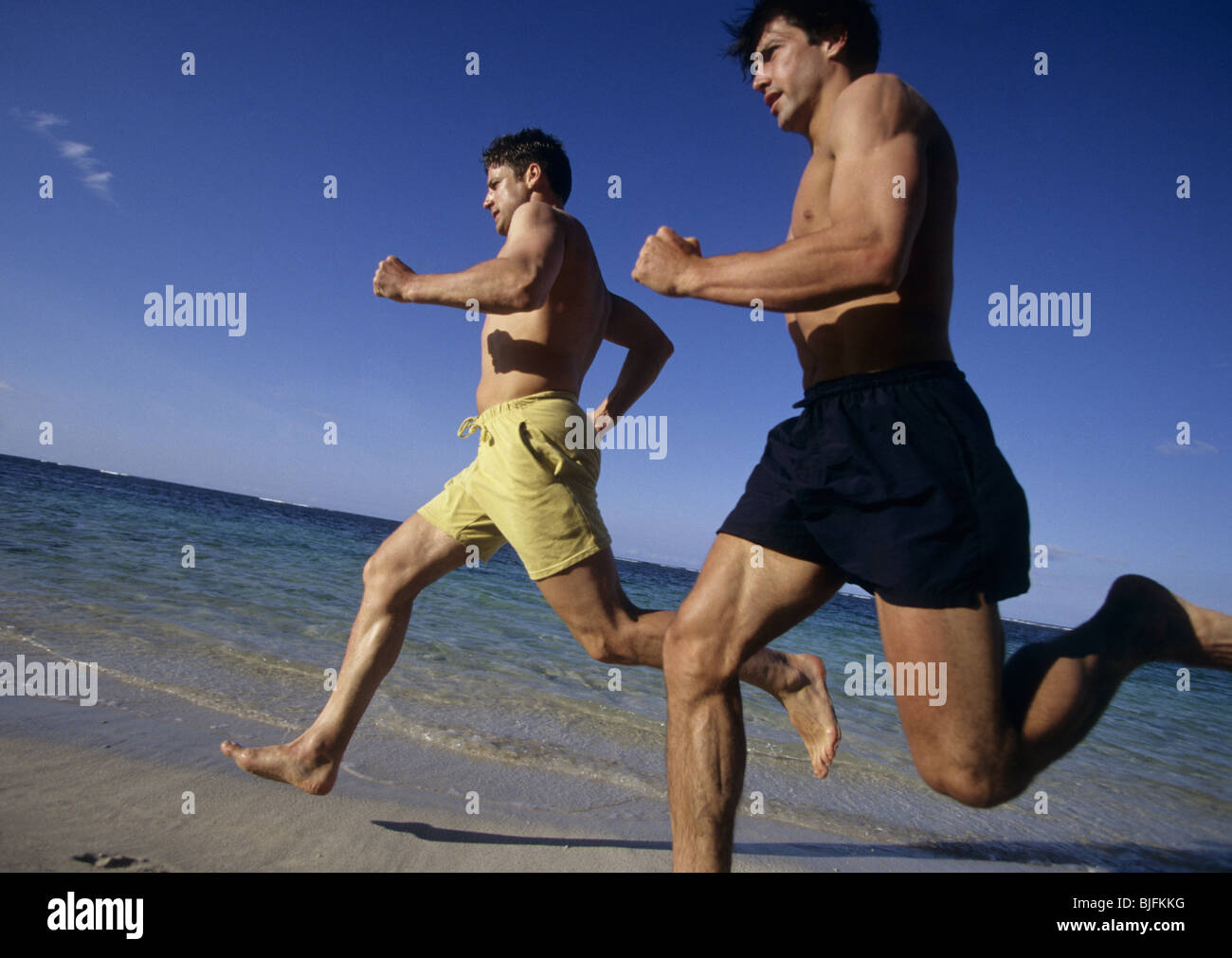 Two men running along a beach by the water Stock Photo - Alamy