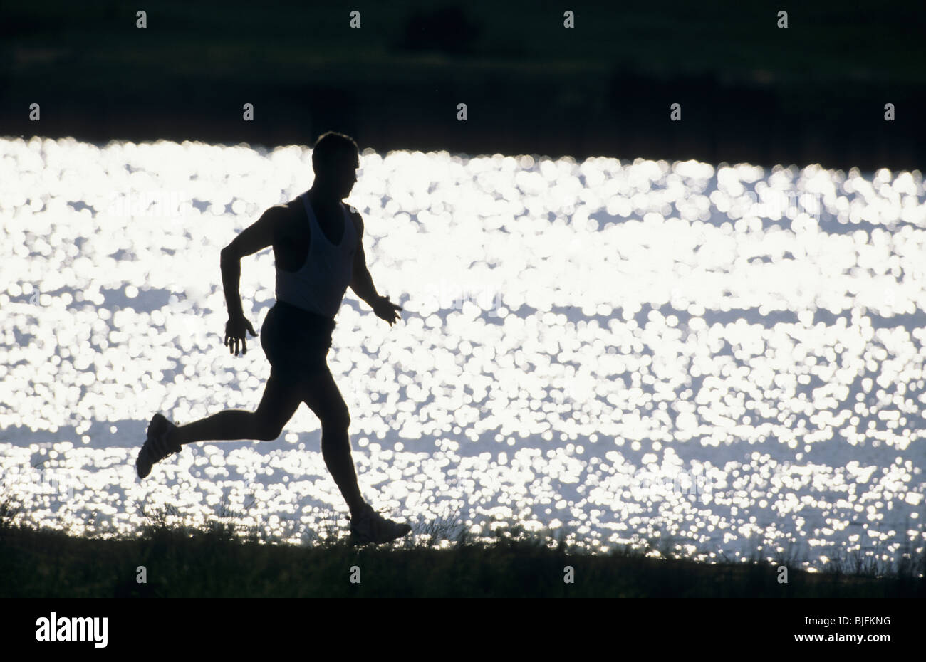 Silhouette of a man running by the side of a lake Stock Photo - Alamy