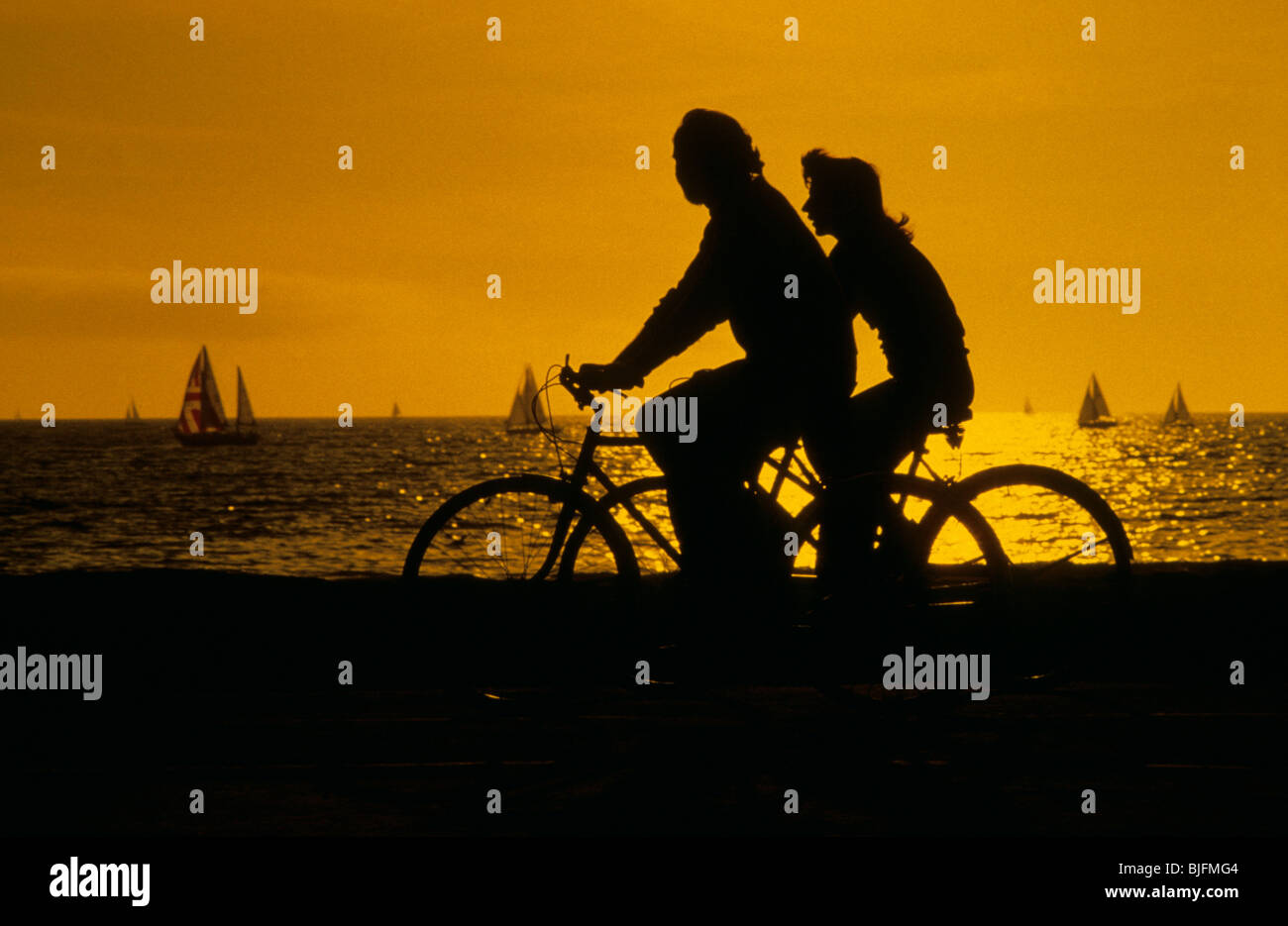 Two people riding bikes by the beach Stock Photo - Alamy