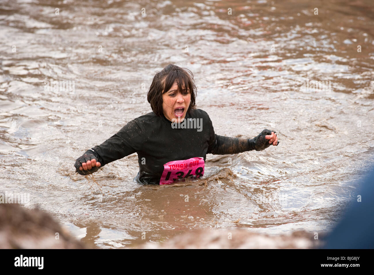 Young female cross country runner wading chest deep in cold muddy water ...