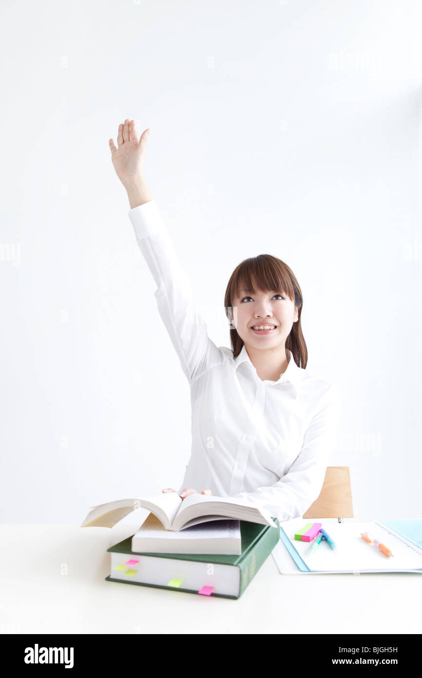 Young woman raises her hand while studying at her desk Stock Photo - Alamy