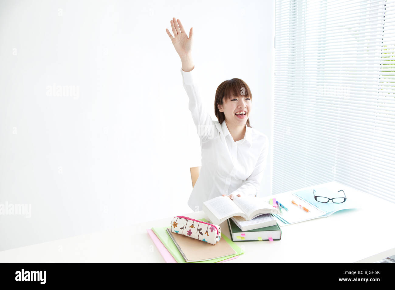 Young woman raises her hand while studying at her desk Stock Photo - Alamy