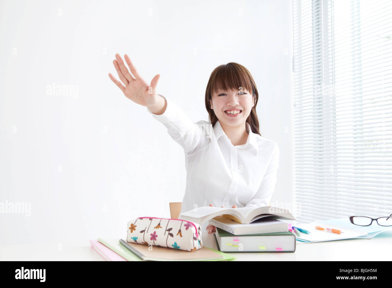 Young woman raises her hand while studying at her desk Stock Photo - Alamy