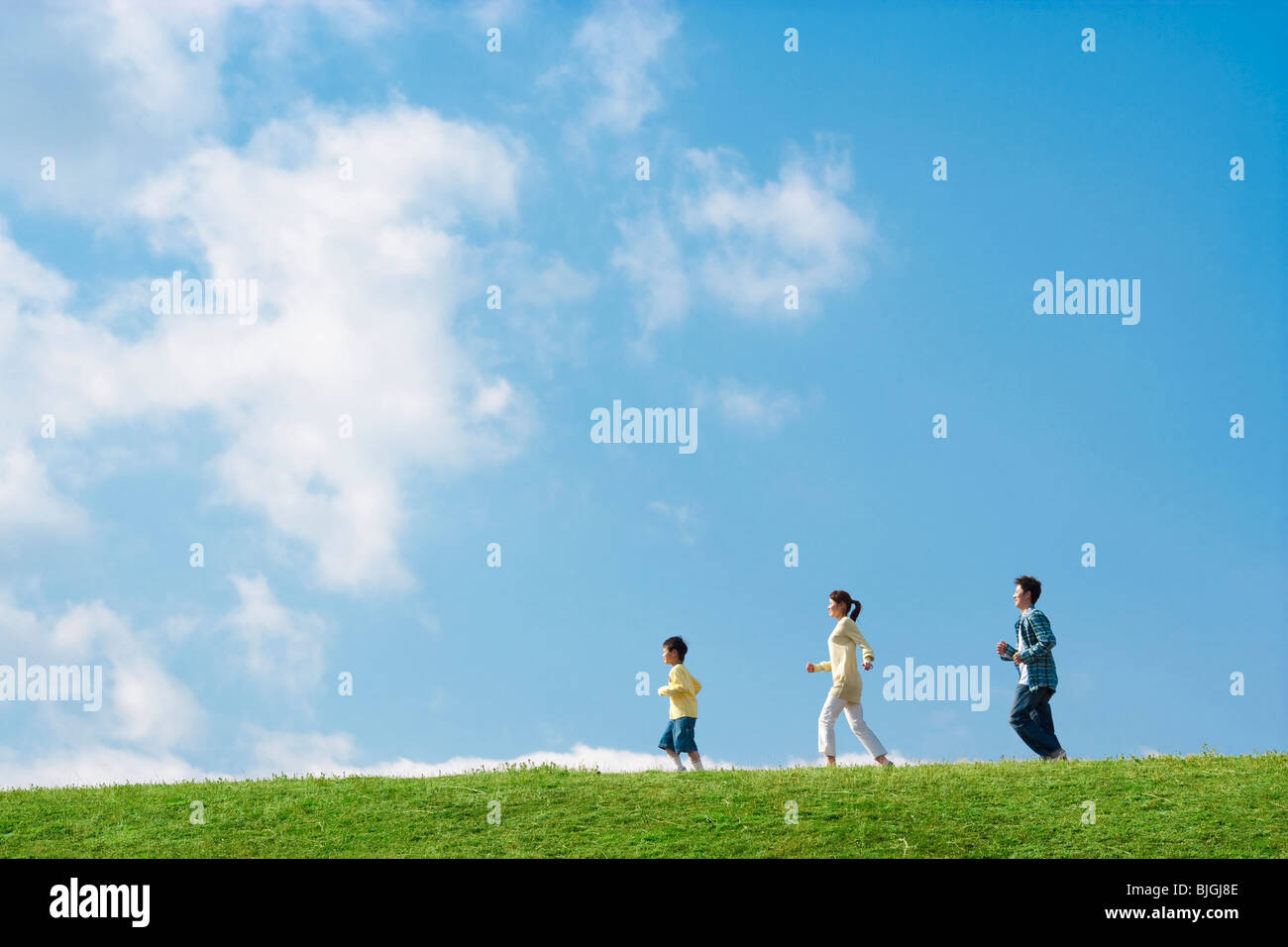 Side view of a family with young son running in the park against a blue ...