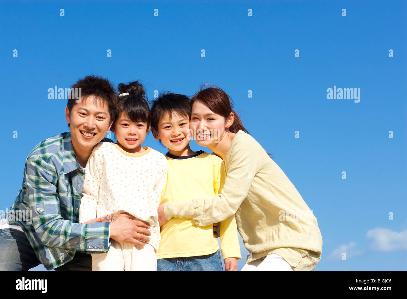 Portrait of a family of four hugging against a blue sky Stock Photo - Alamy
