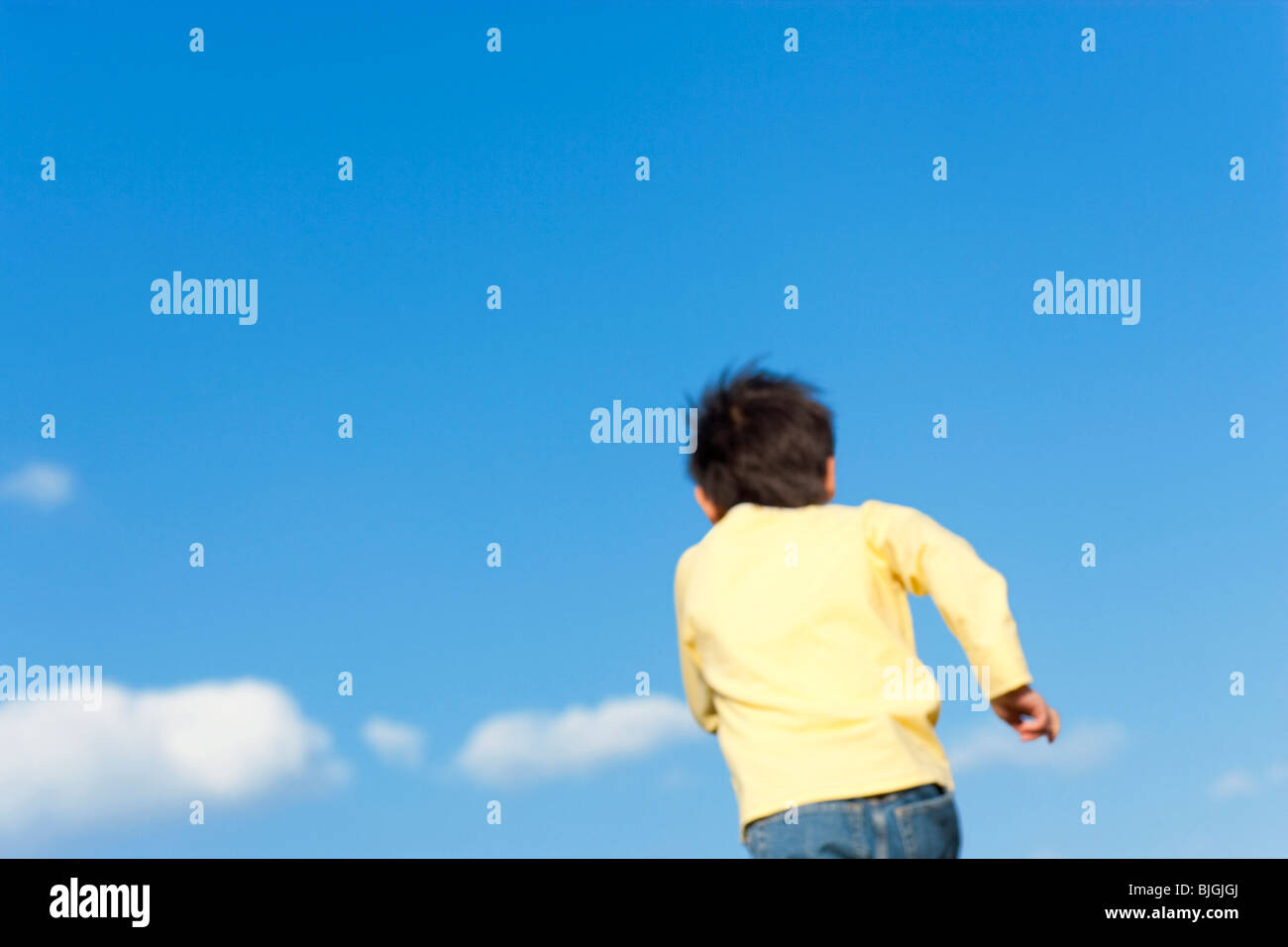 Rear view of young boy running against a blue sky Stock Photo - Alamy