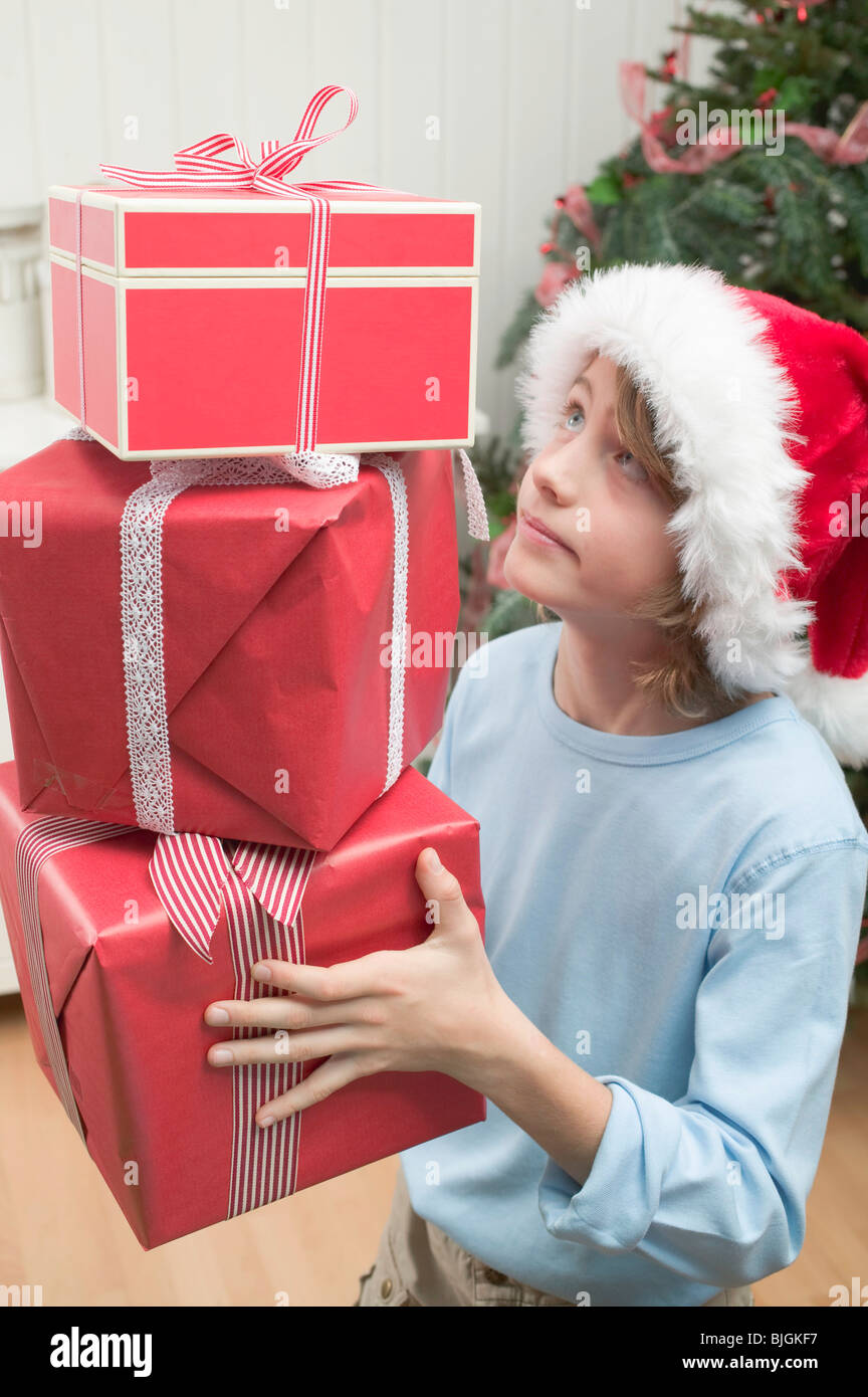 Boy in Father Christmas hat carrying pile of parcels Stock Photo - Alamy