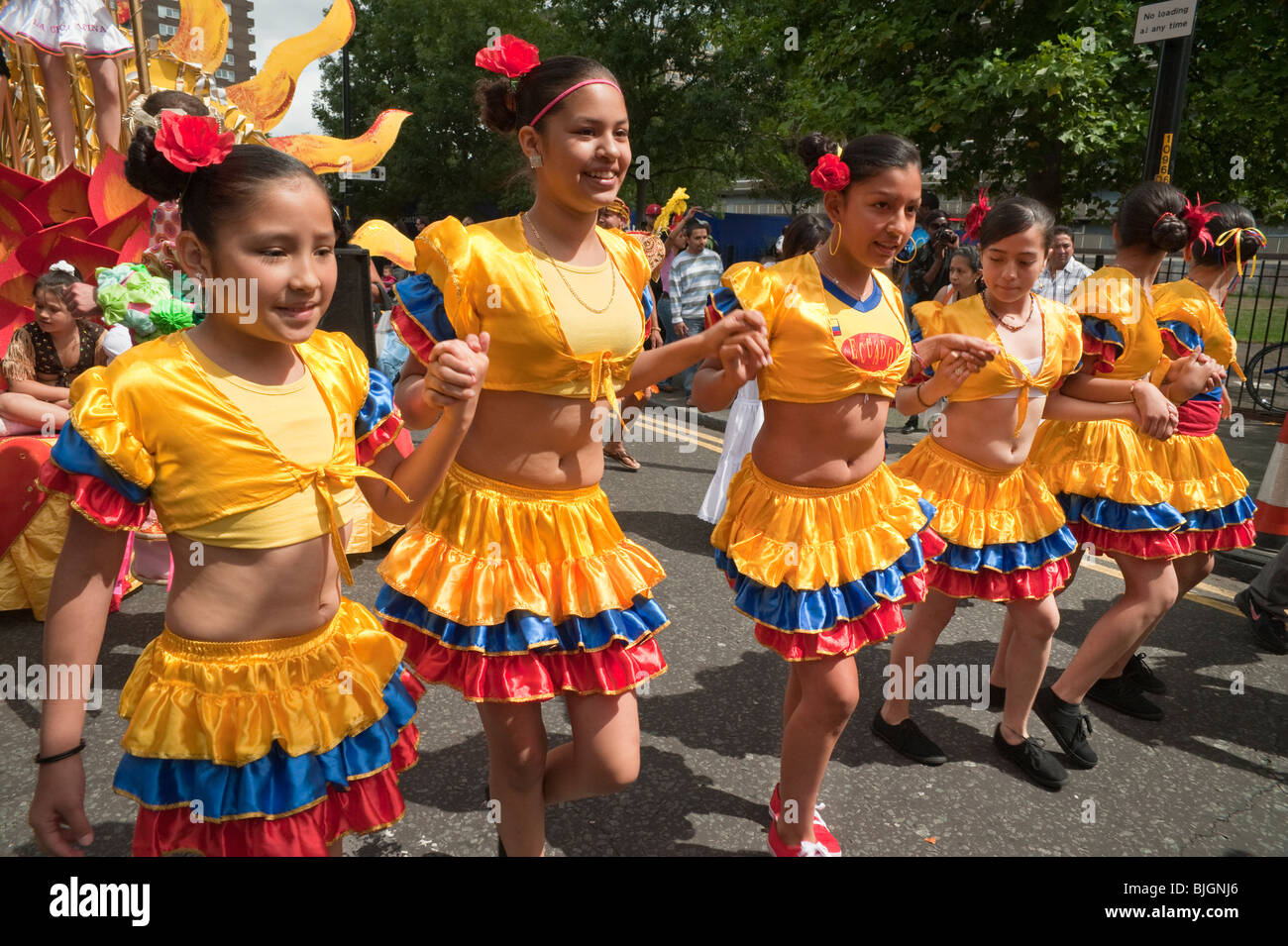 A line of young girls in bright yellow blue and red dancing at Carnaval ...