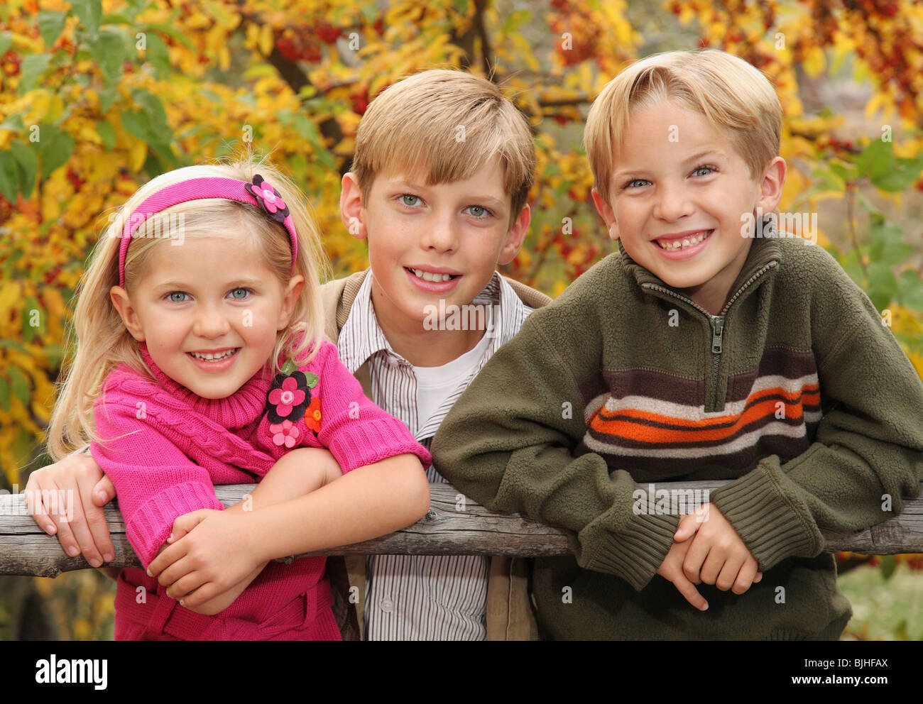 three cute siblings together outside with colorful fall background ...