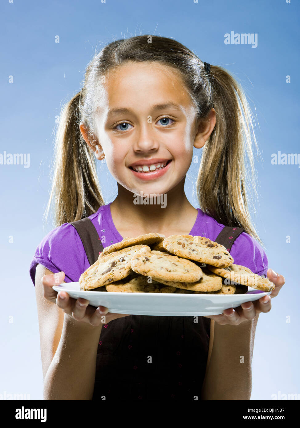 girl looking at the camera holding a plate of chocolate chip cookies ...