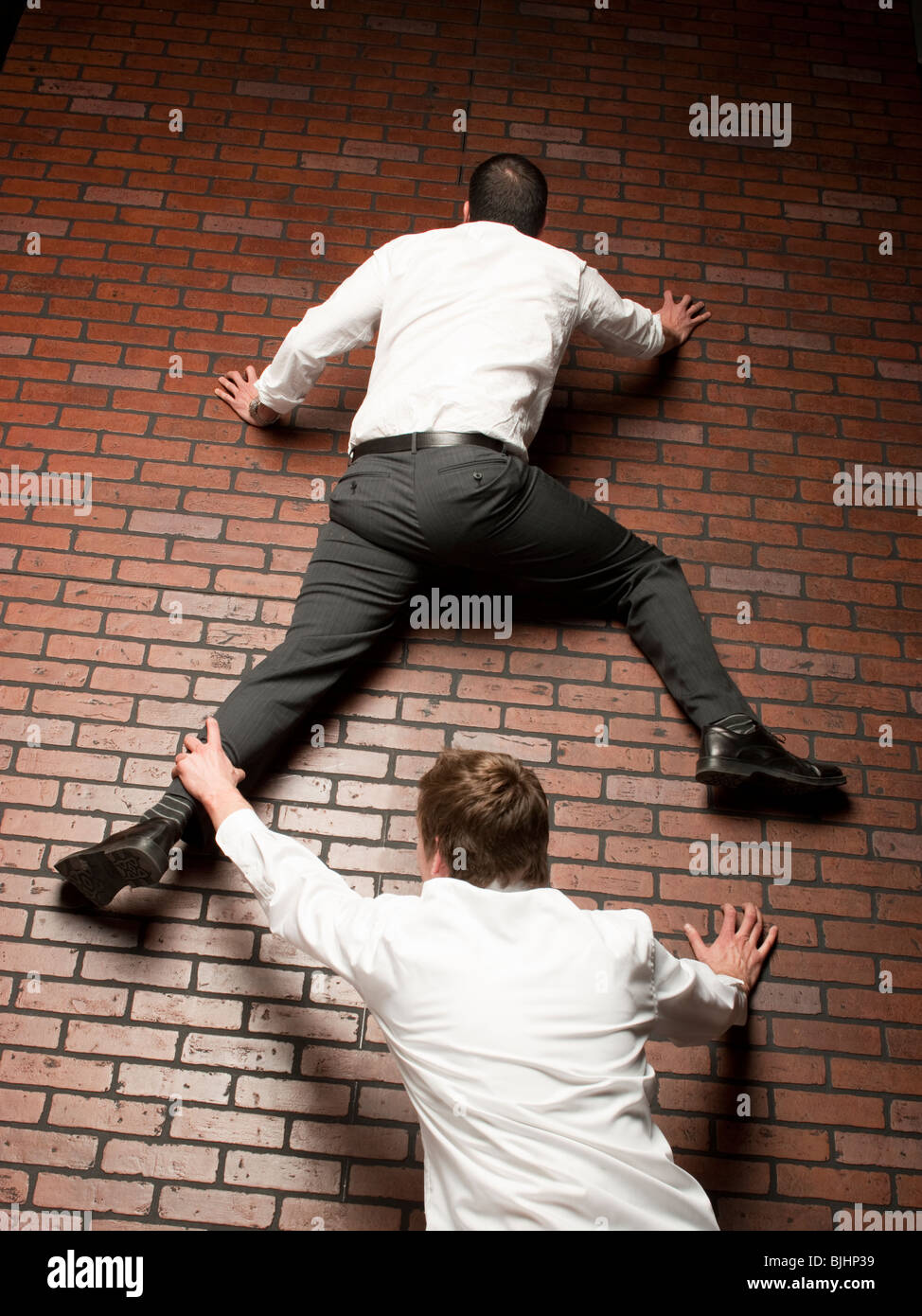 man climbing up a brick wall while another man grabs on to his leg ...