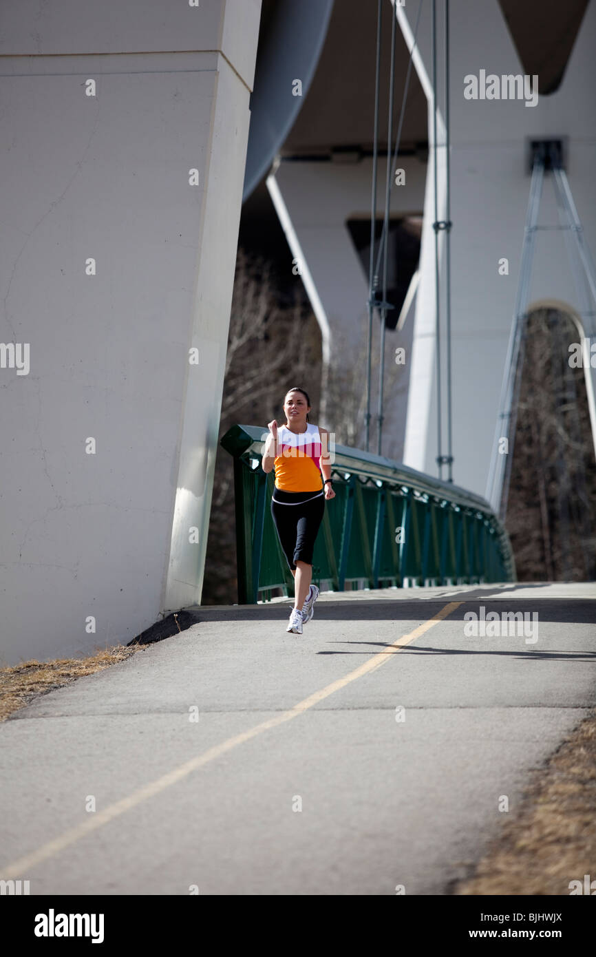 Fit young woman jogging on pedestrian bridge and city pathway Stock ...