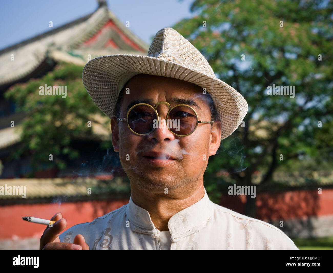 Man with sunglasses and straw hat smoking cigarette outdoors with ...