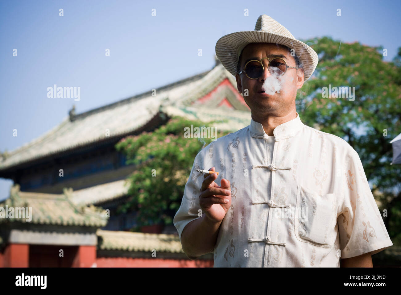 Man with sunglasses and straw hat smoking cigarette outdoors with ...