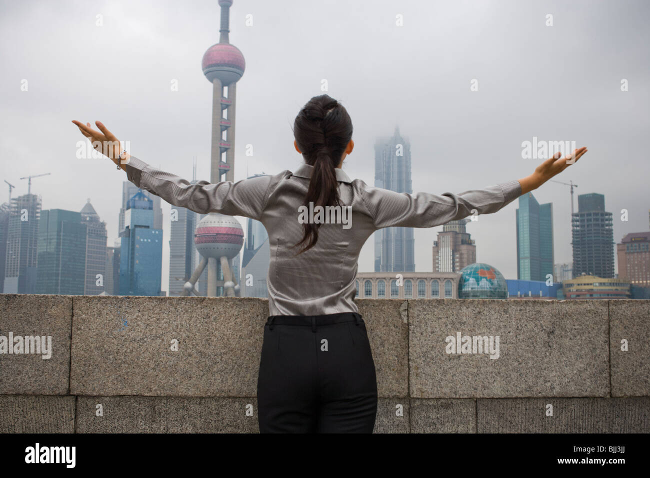 Businesswoman outdoors with arms up and city skyline in background rear ...