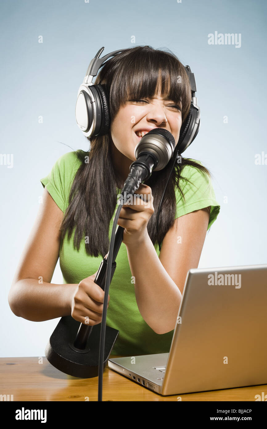 Young woman recording into a microphone with headphones and a laptop ...