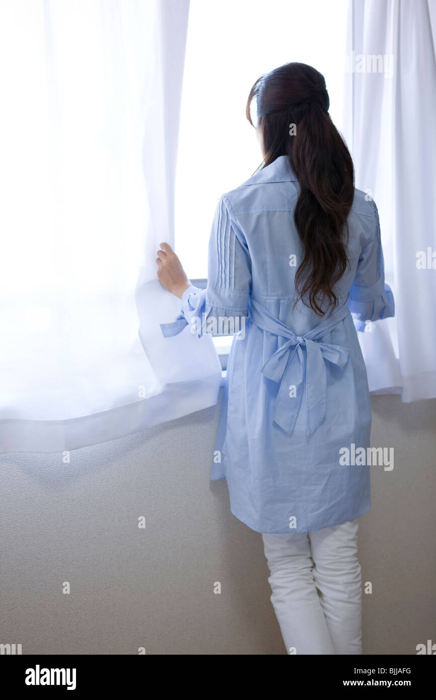 Young woman looking through window Stock Photo - Alamy
