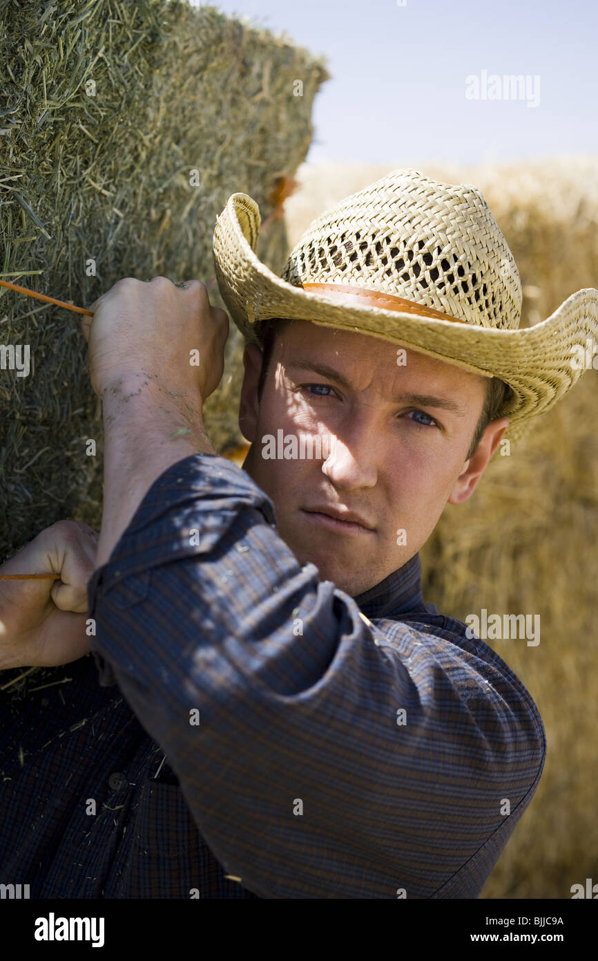 Man in cowboy hat carrying bales of hay smiling Stock Photo - Alamy