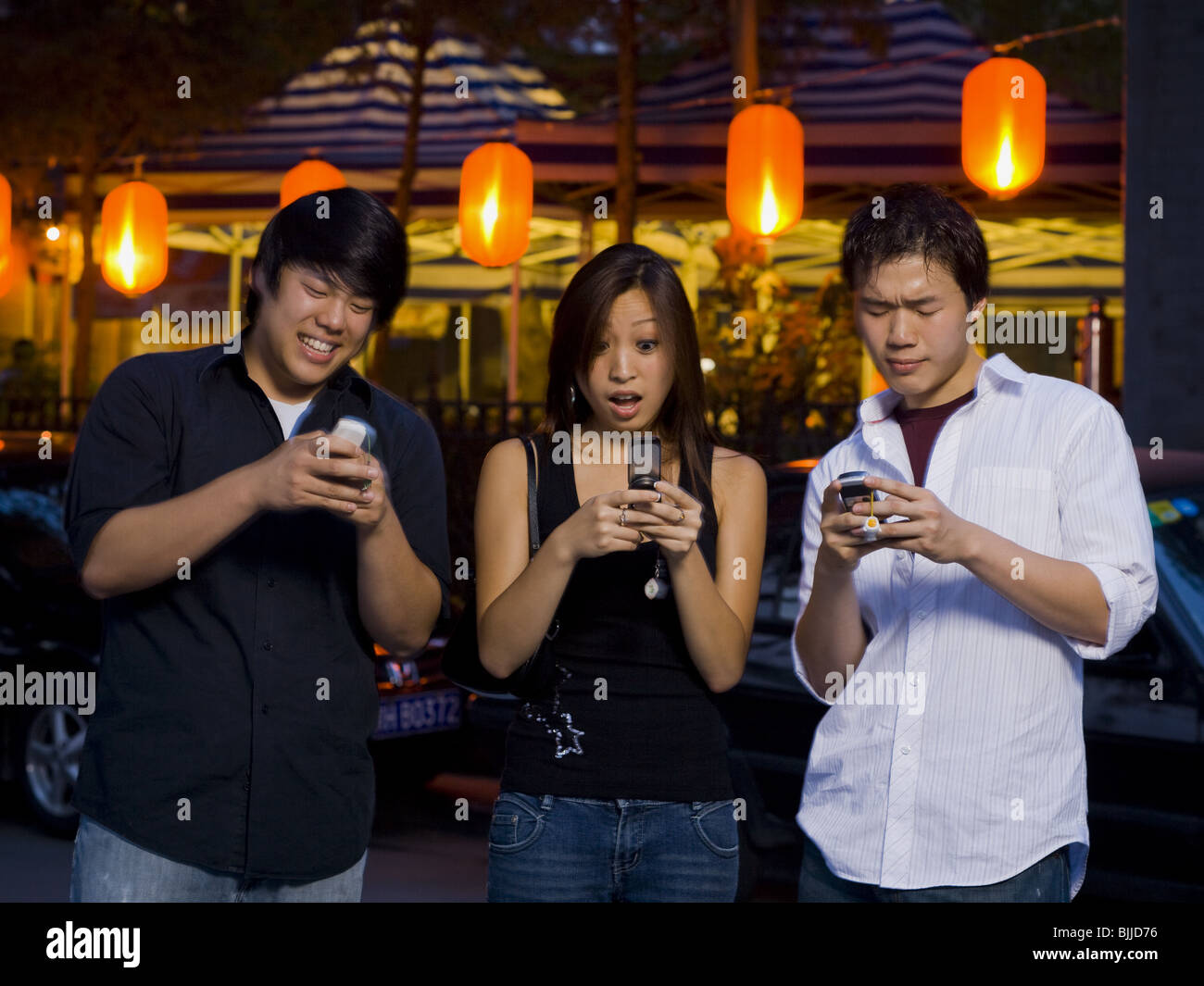 Three people with cell phones outdoors at night smiling Stock Photo - Alamy