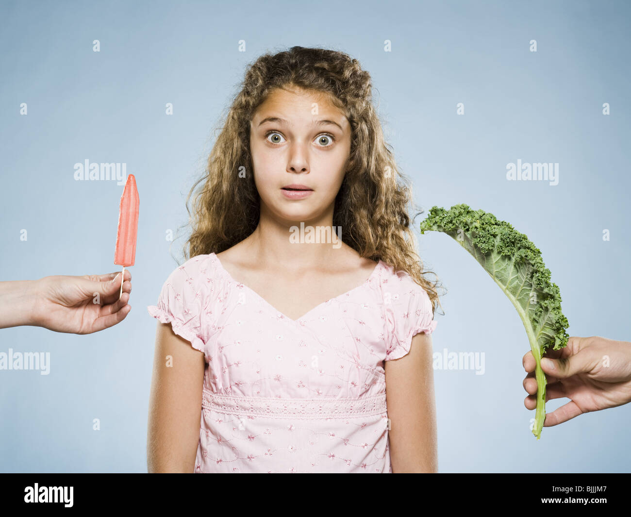 Girl deciding between Popsicle and green leafy vegetable Stock Photo ...