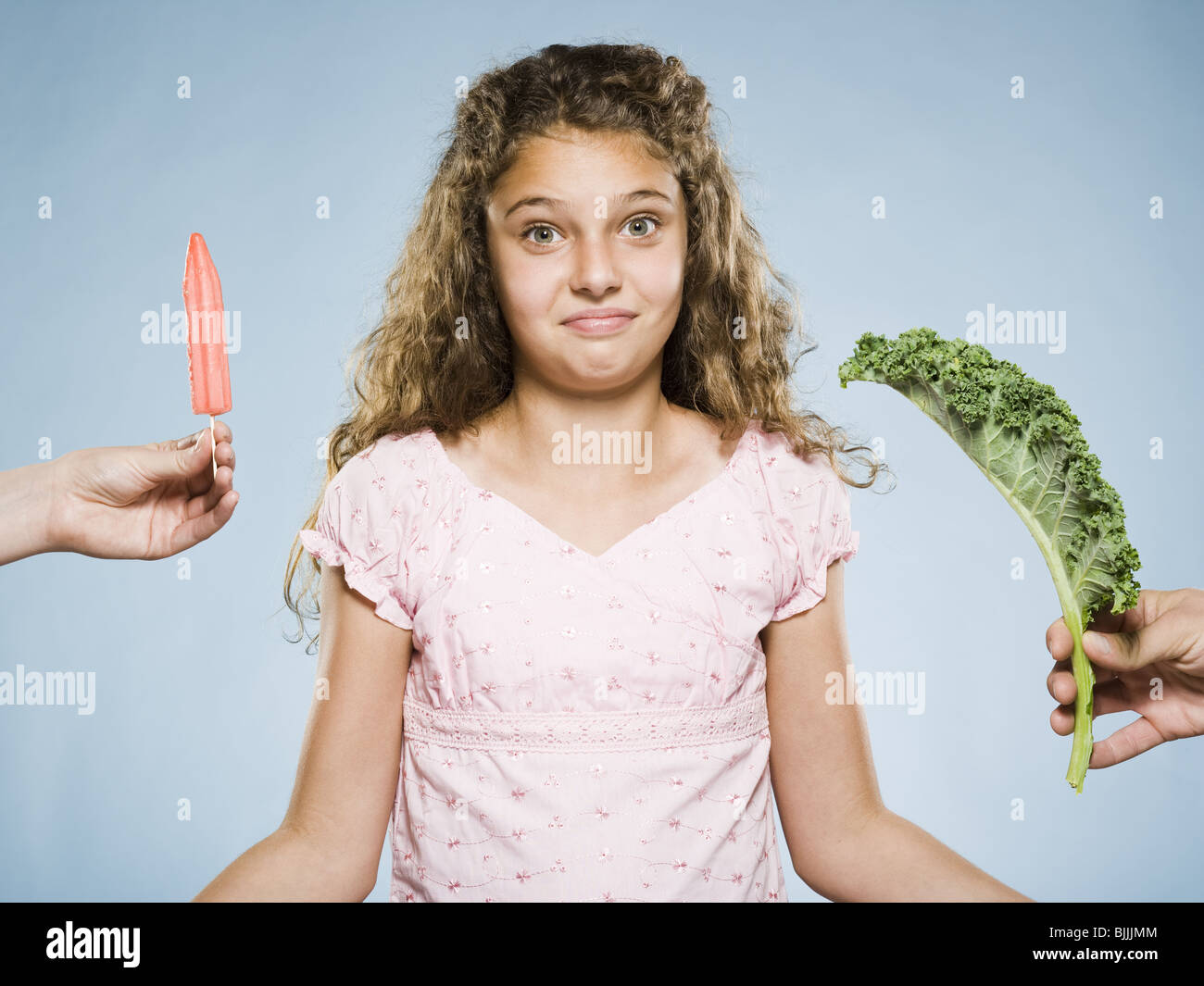 Girl deciding between Popsicle and green leafy vegetable Stock Photo ...