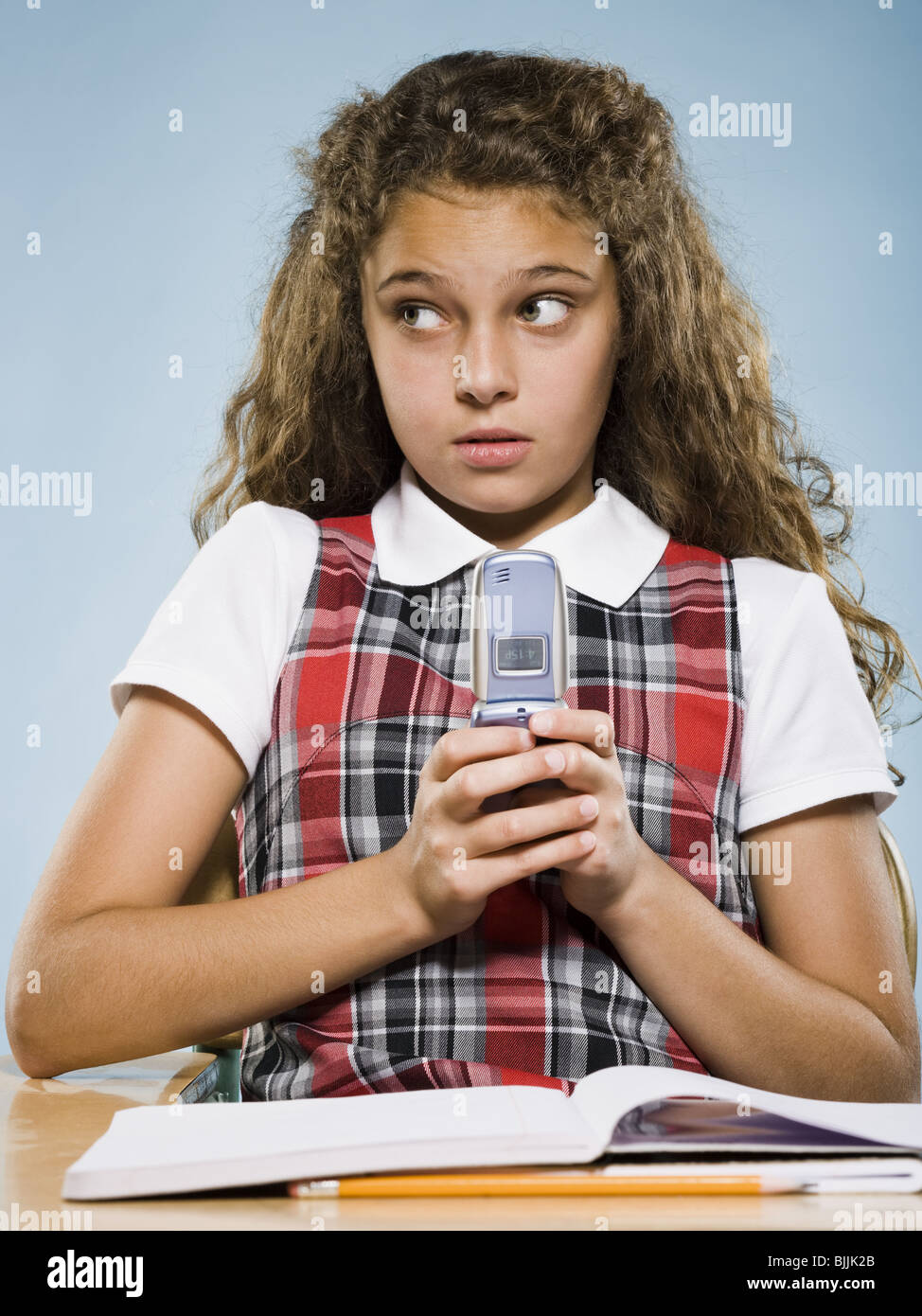 Girl sitting at desk with workbook hiding cell phone Stock Photo - Alamy