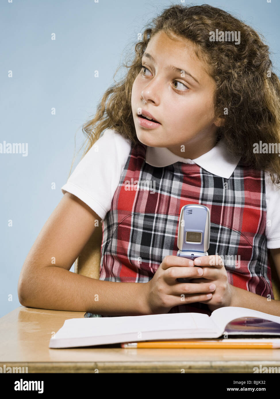 Girl sitting at desk with workbook hiding cell phone Stock Photo - Alamy
