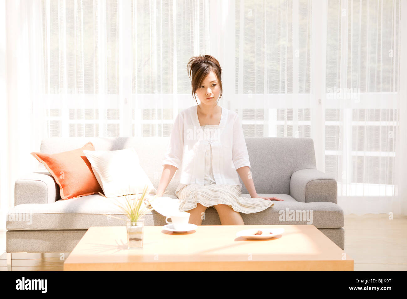 Woman sitting on sofa in living room Stock Photo - Alamy