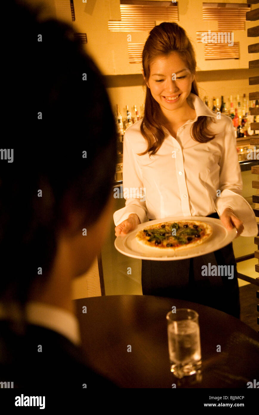Waitress bringing a pizza to a table Stock Photo - Alamy