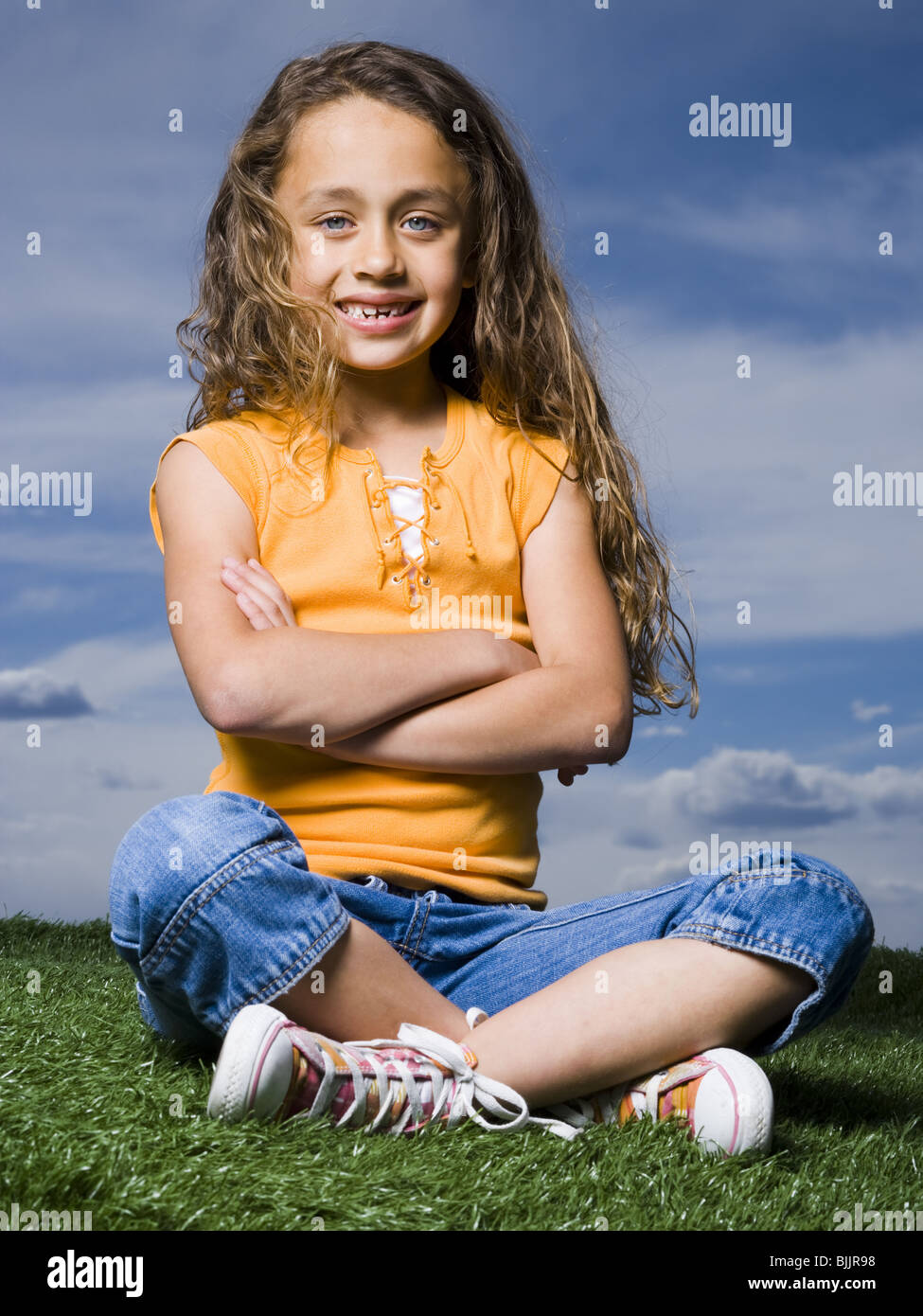 Girl sitting cross legged on grass outdoors with arms crossed smiling ...