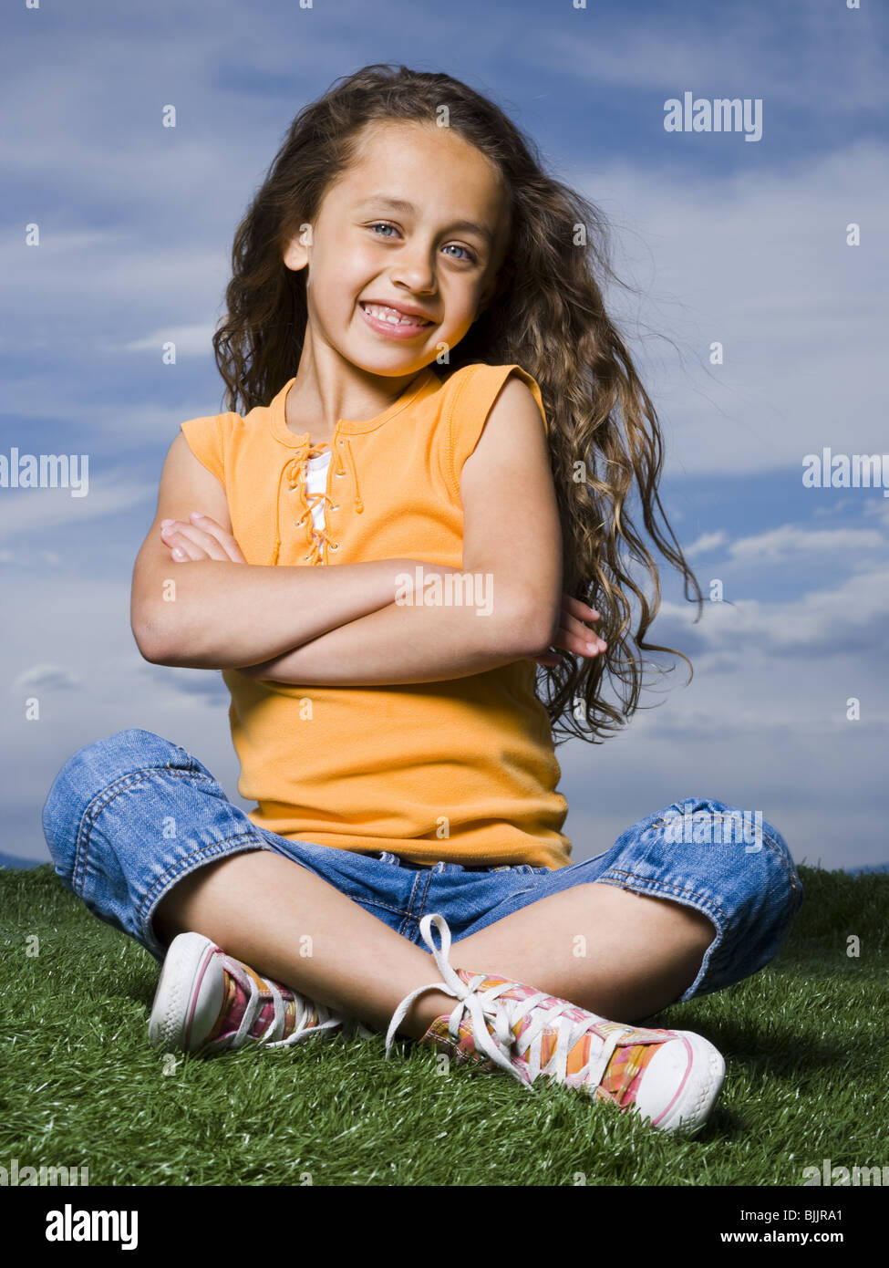 Girl sitting cross legged on grass outdoors with arms crossed smiling ...