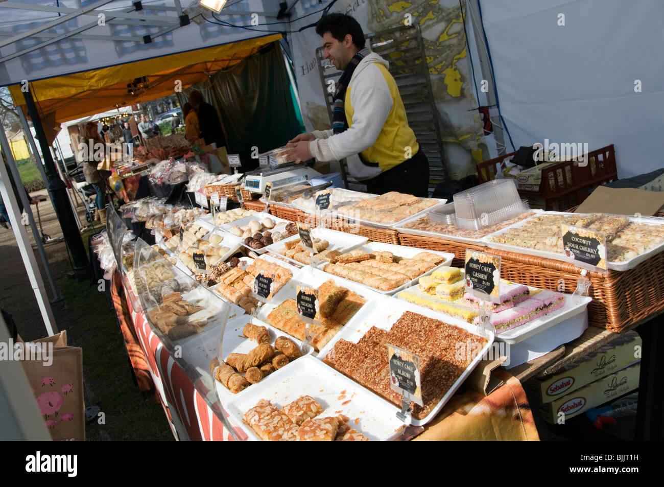 A salesman on a stall with sweet pastries at a French market in England ...