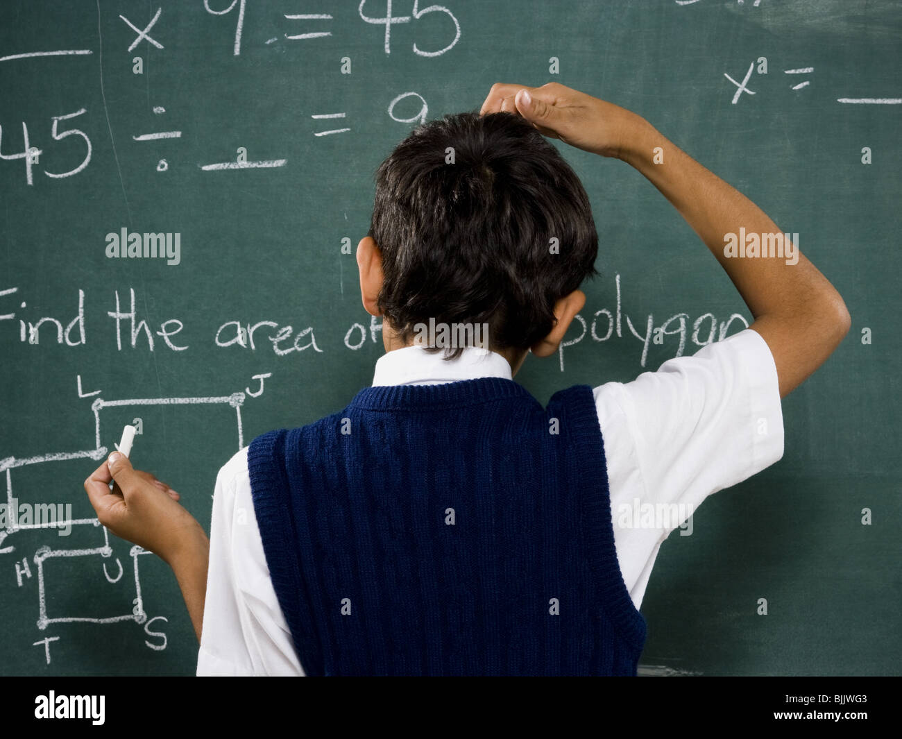 Rear view of boy at chalkboard doing math formulas and scratching head ...