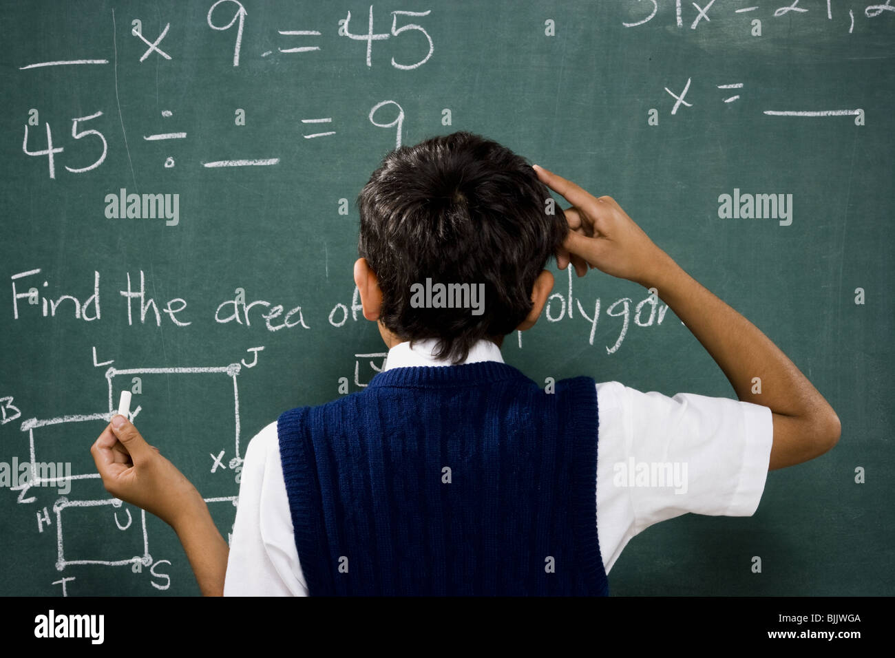 Rear view of boy at chalkboard doing math formulas and scratching head ...