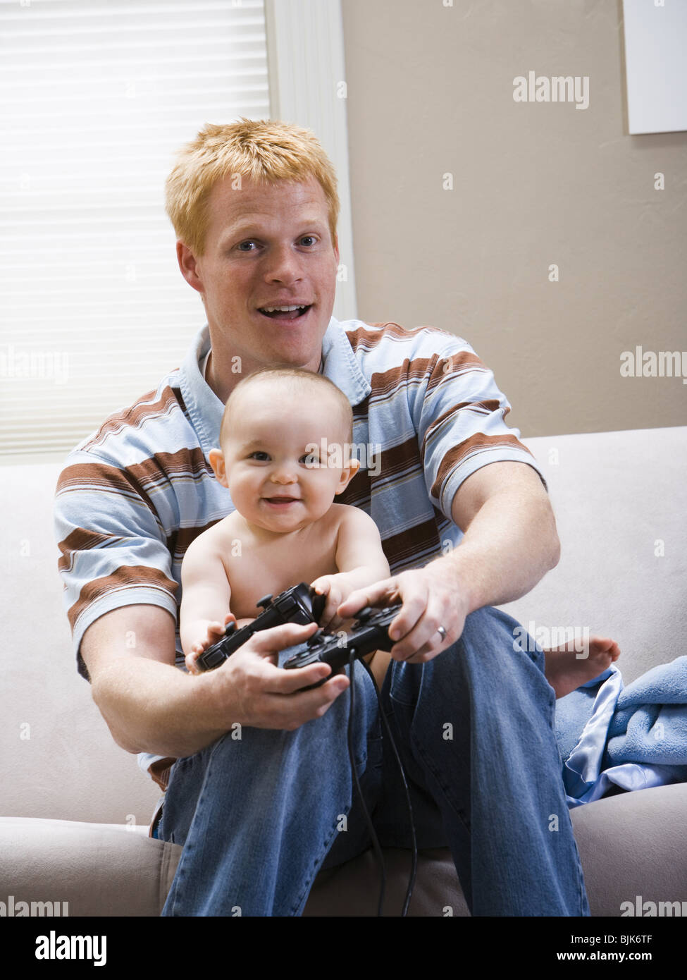 Man and baby on sofa with video game controller smiling Stock Photo - Alamy