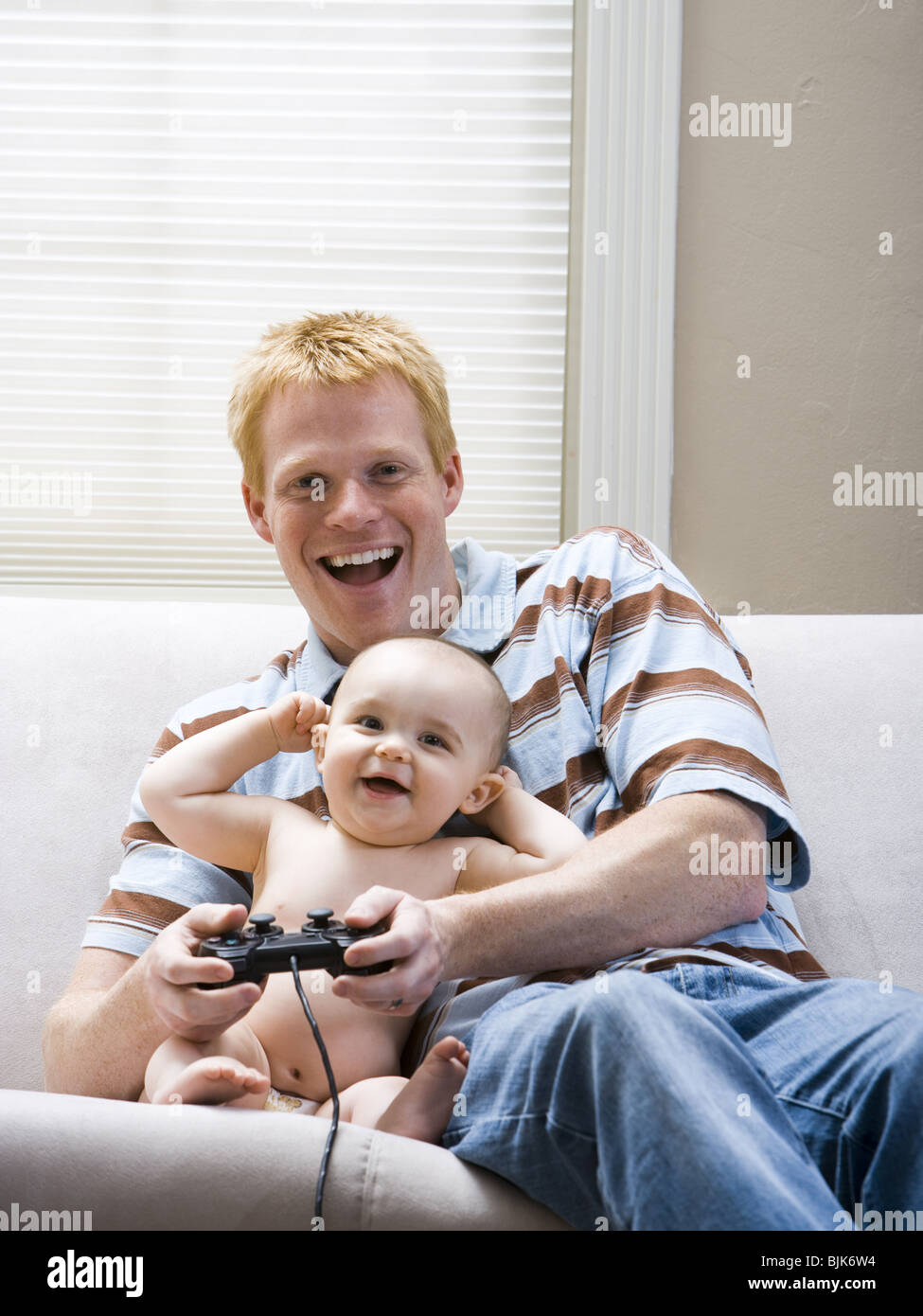 Man and baby on sofa with video game controller smiling Stock Photo - Alamy