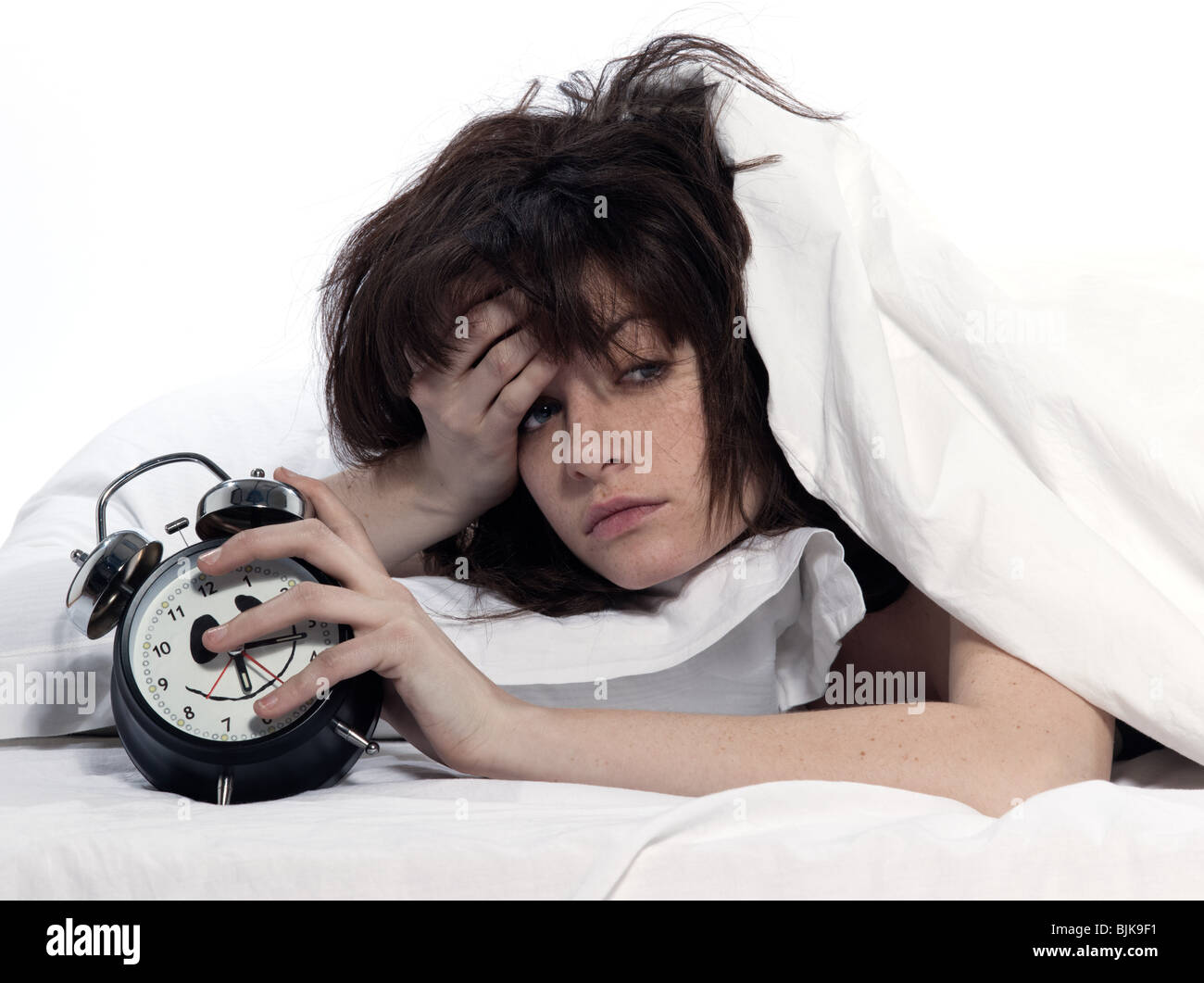 young woman woman in bed awakening tired holding alarm clock on white ...