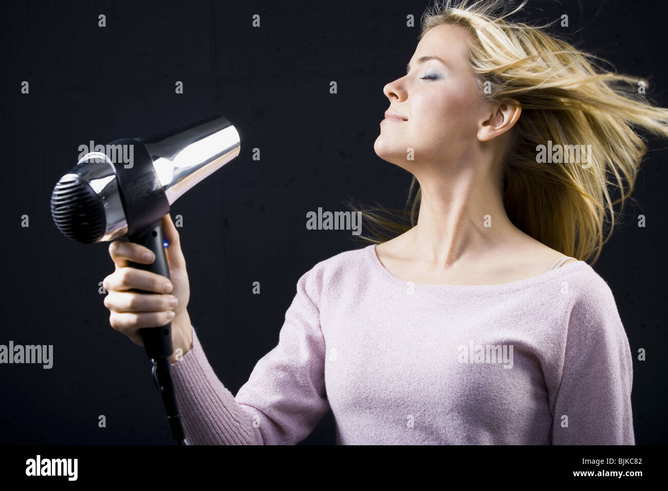 Woman blow drying blonde hair with closed eyes Stock Photo - Alamy