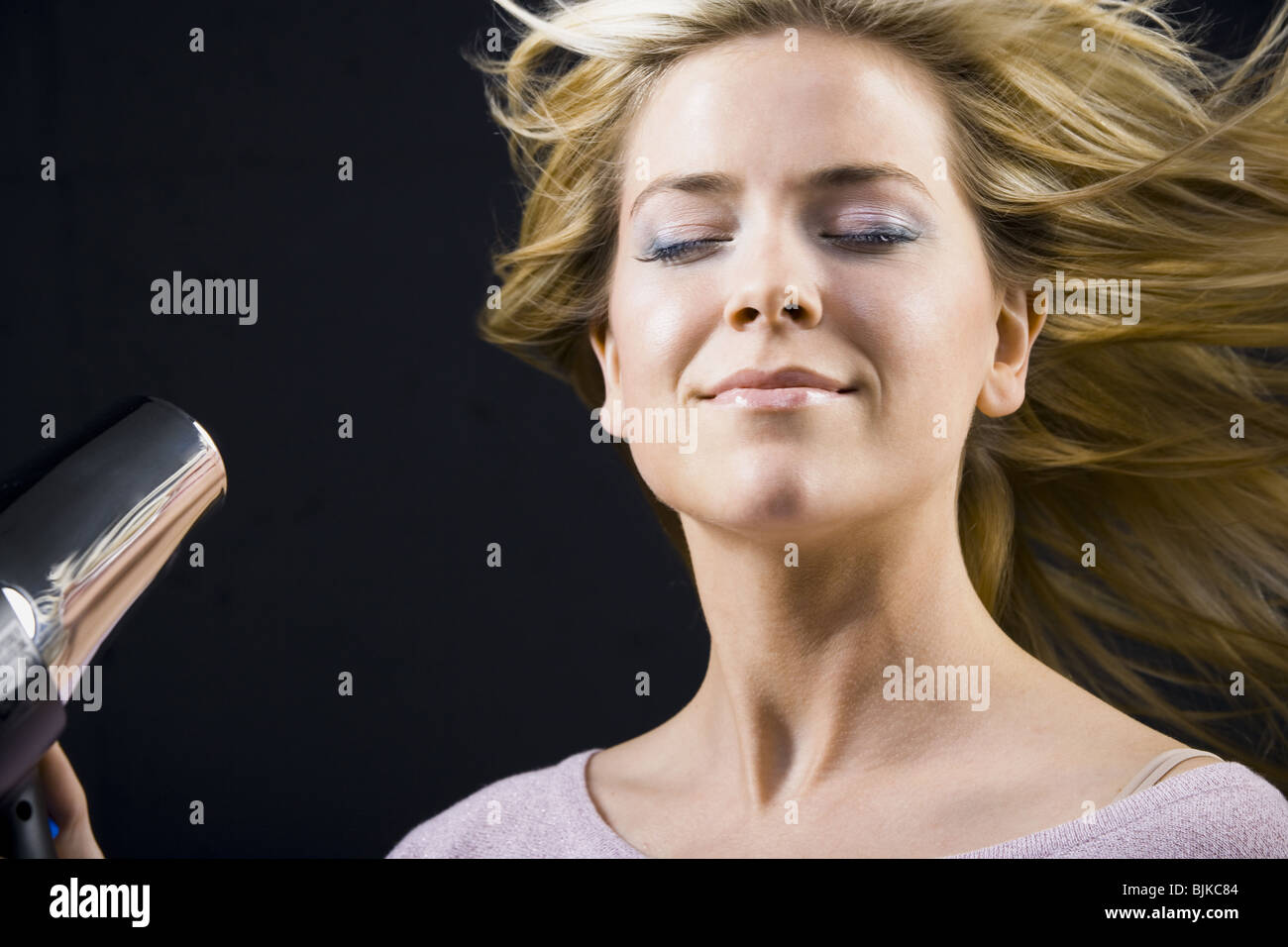 Woman blow drying blonde hair with closed eyes Stock Photo - Alamy