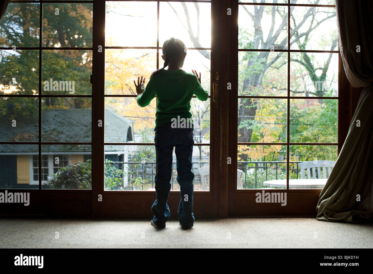 Young girl looking through large window Stock Photo - Alamy