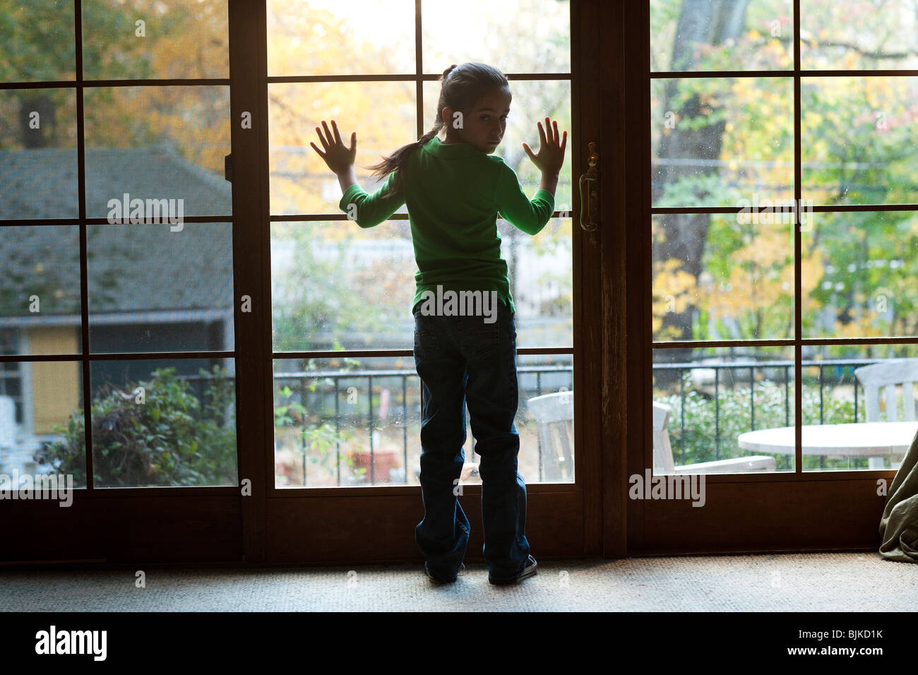 Young girl looking through large window Stock Photo - Alamy