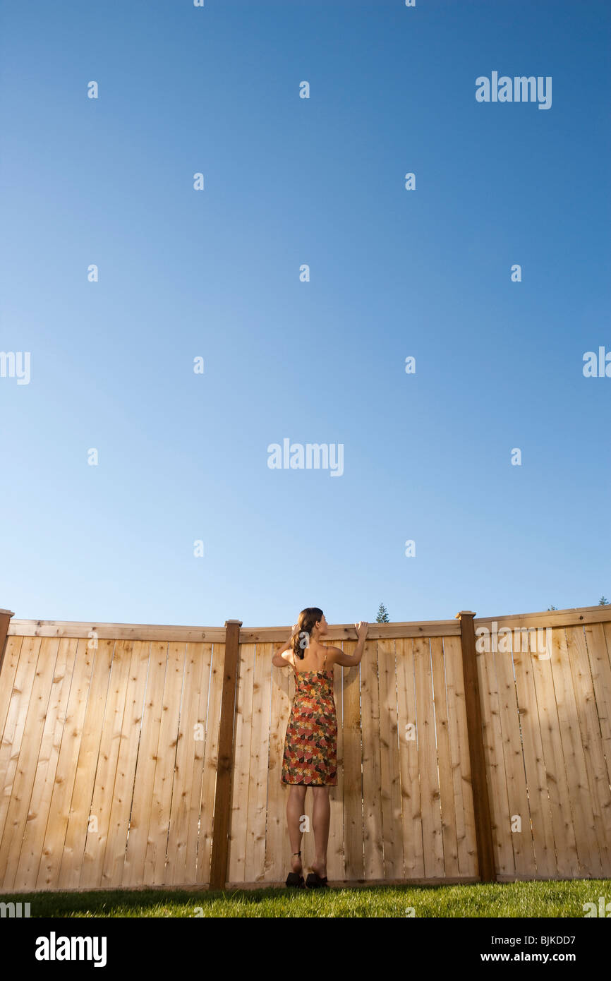 Woman standing on chair peeping over fence Stock Photo - Alamy