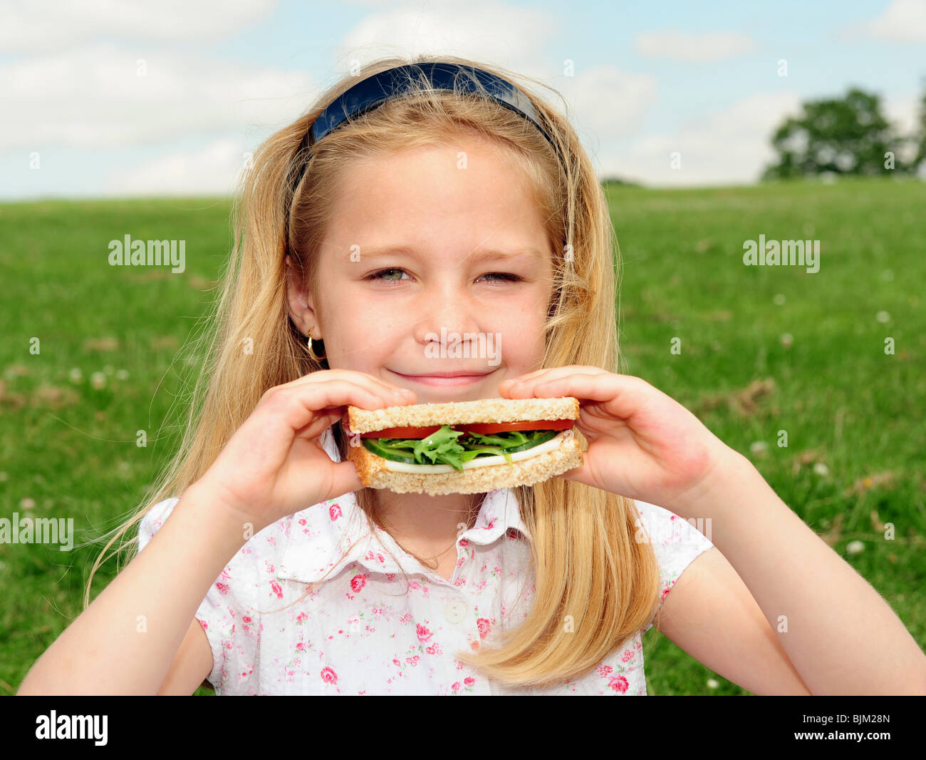 Horizontal image of a young girl eating a healthy sandwich in the park ...